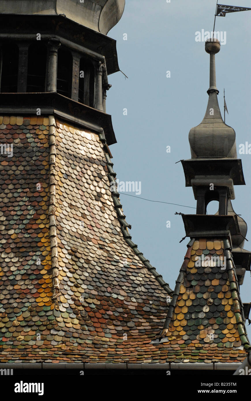 Medieval steep roof with multi-coloured tiles of a clock tower in a ...