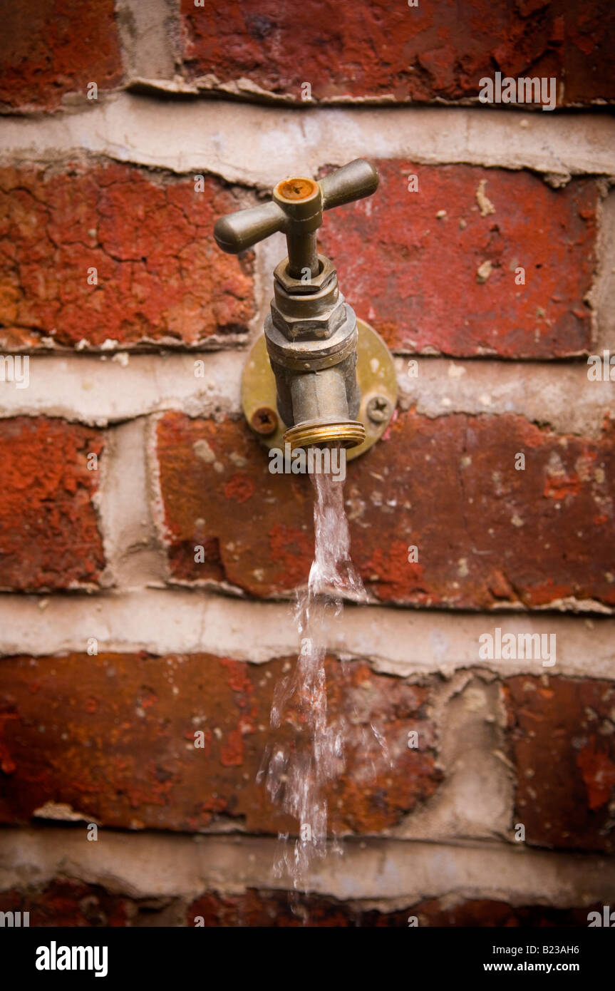 Traditional open tap with running water on a brick wall outdoors Stock ...