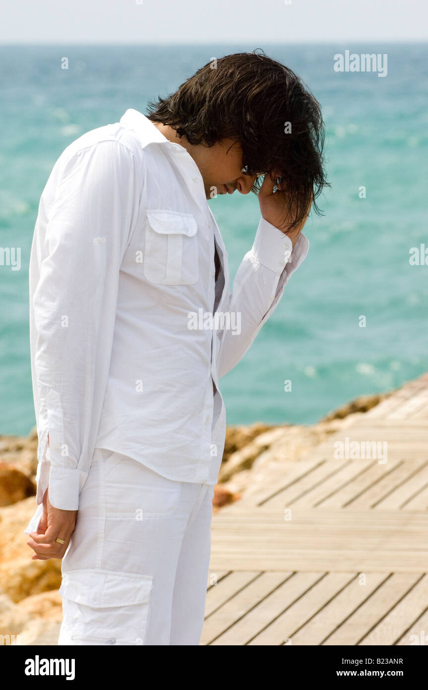 Man wearing white standing by the sea head in hand Stock Photo - Alamy