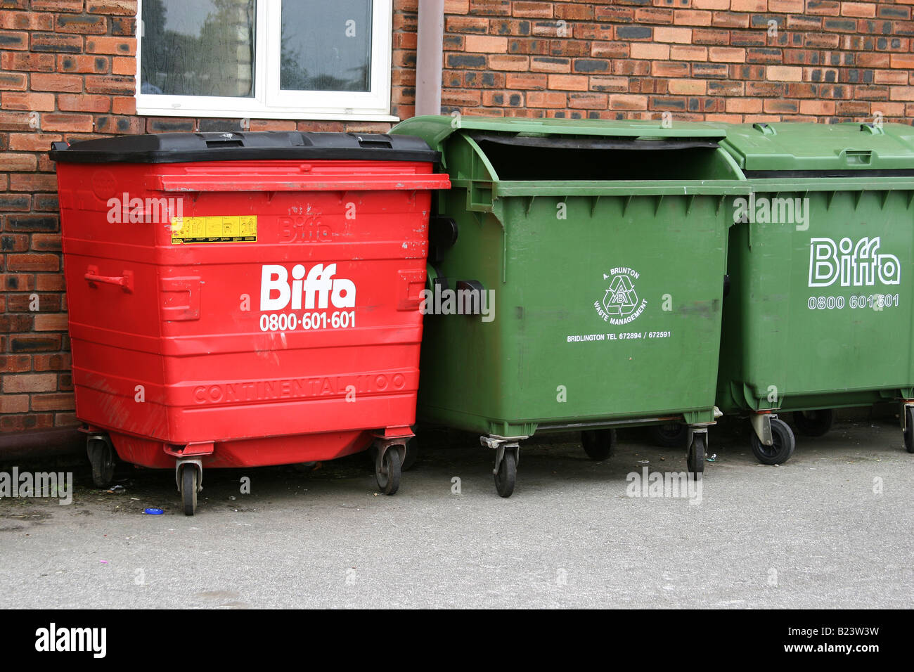 Waste roller type trade skips lined up outside public house brick wall ...