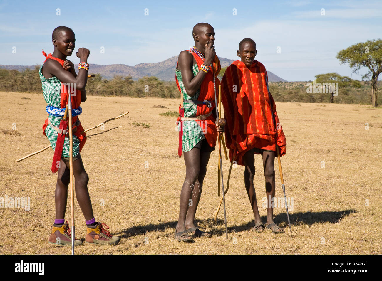 Smiling young male Masai Warriors carrying spears dressed in bright ...