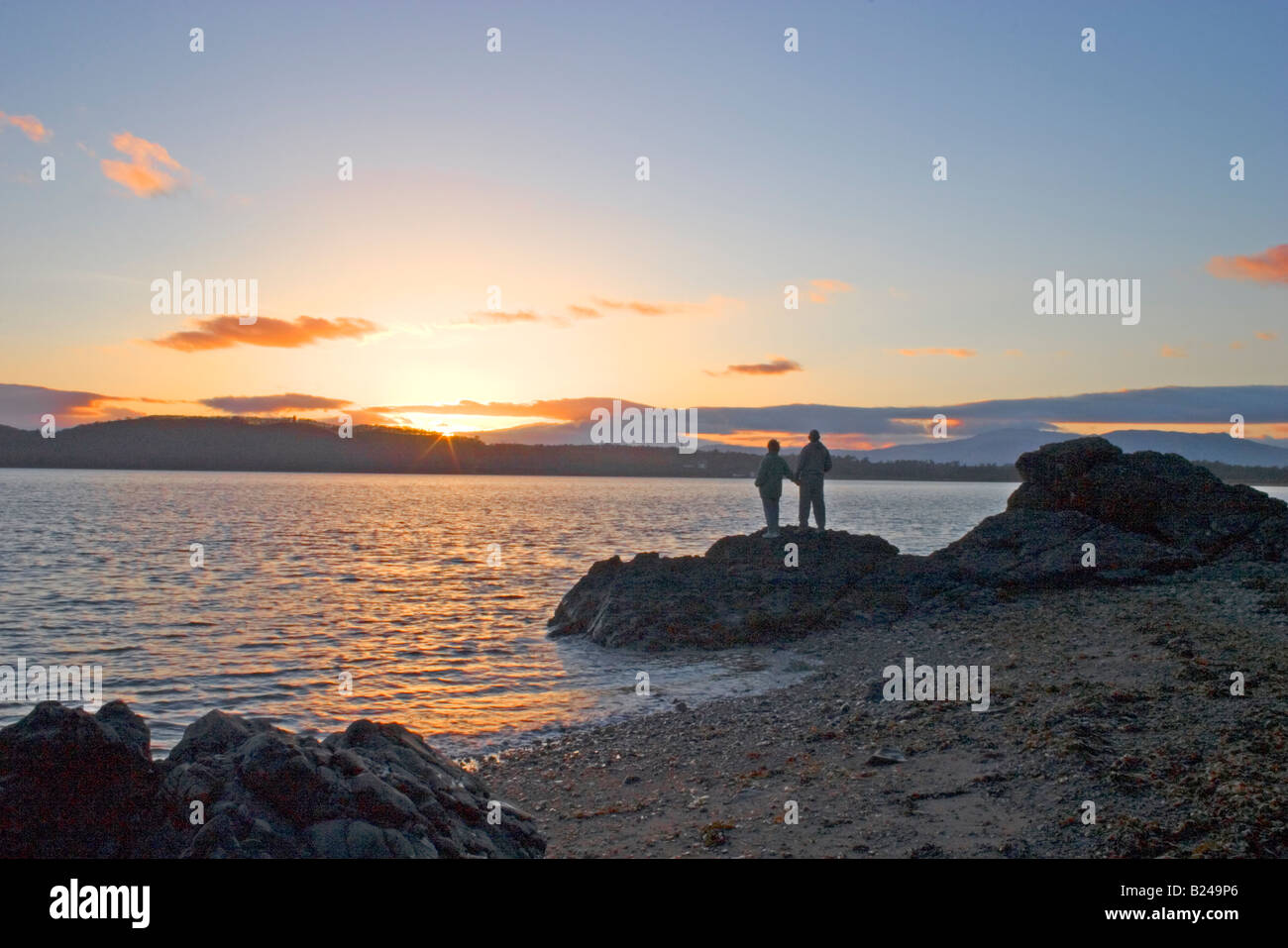 Two people watching setting sun Stock Photo - Alamy