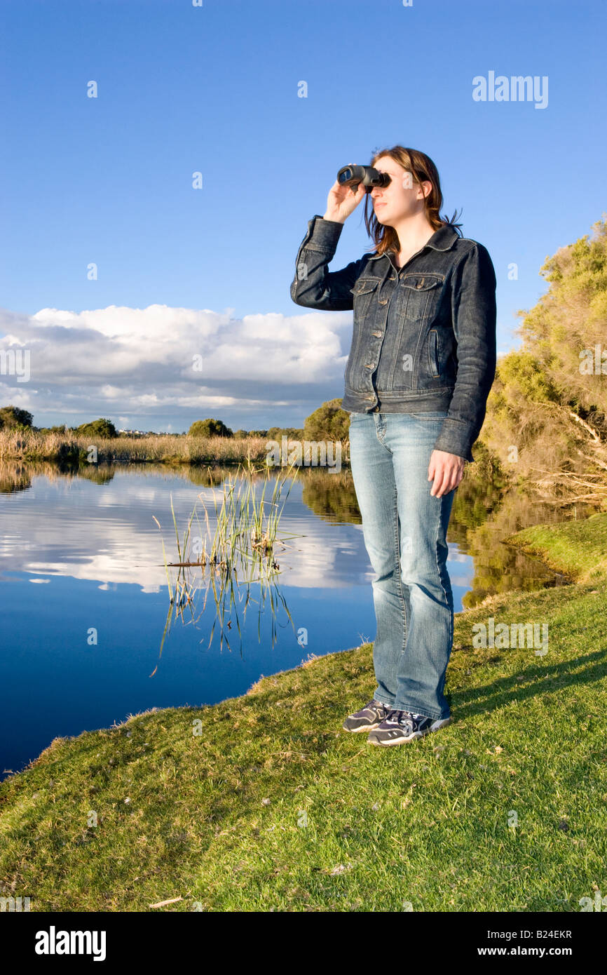 A woman stood beside a lake birdwatching with binoculars Stock Photo ...