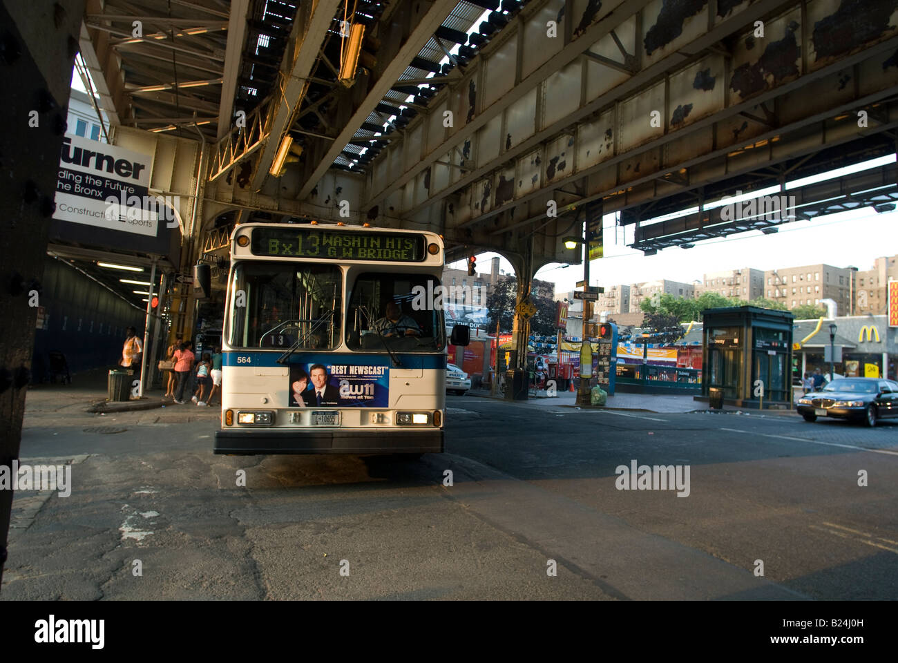 A New York City MTA bus maneuvers a turn under elevated train tracks in ...