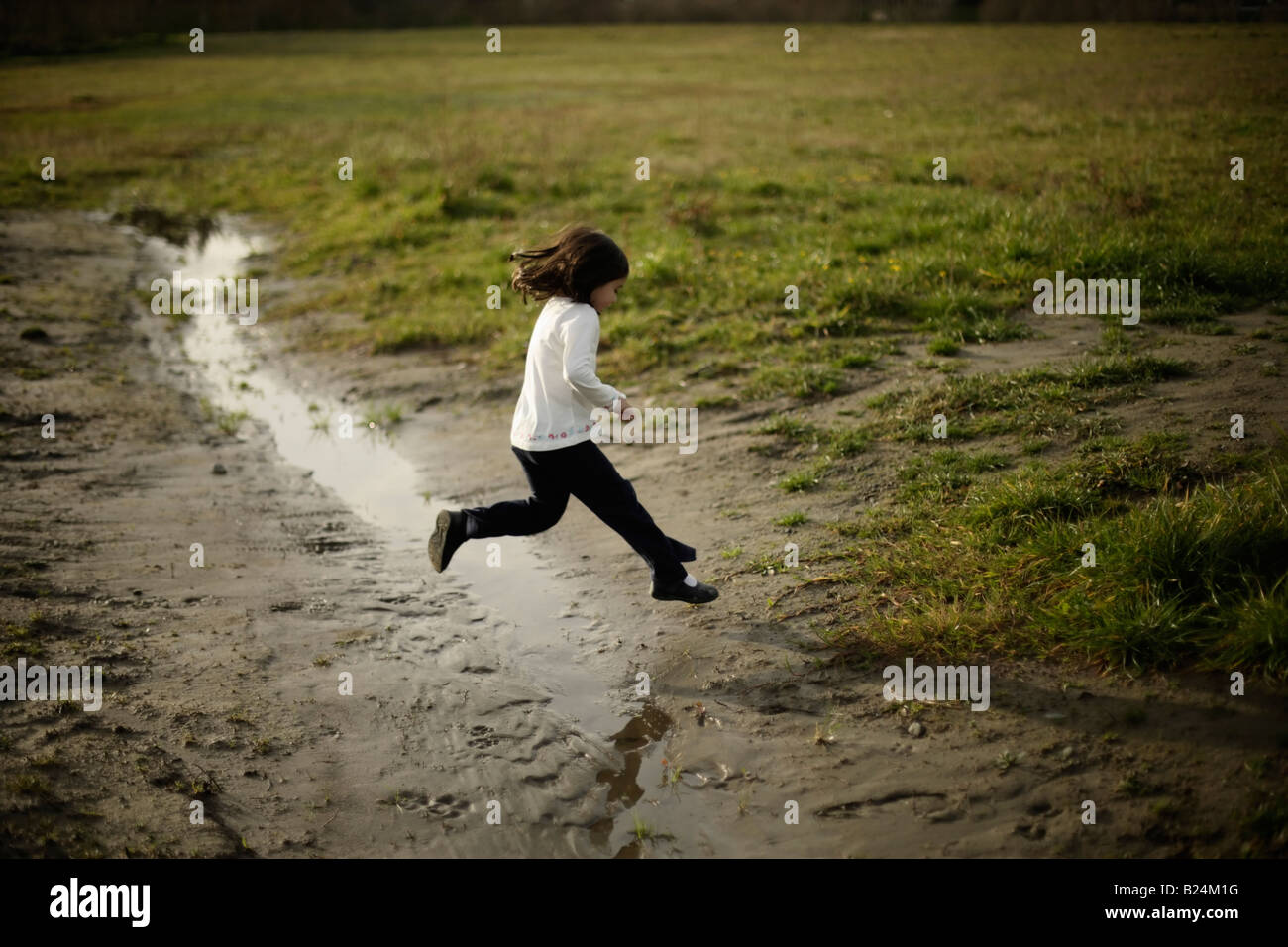 Girl aged five leaps across muddy puddle Stock Photo - Alamy