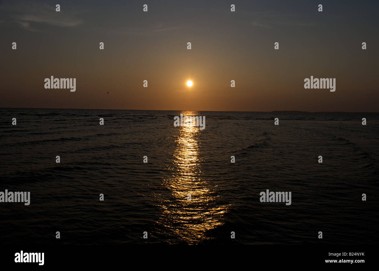 sun setting above the water with reflections in water Stock Photo - Alamy
