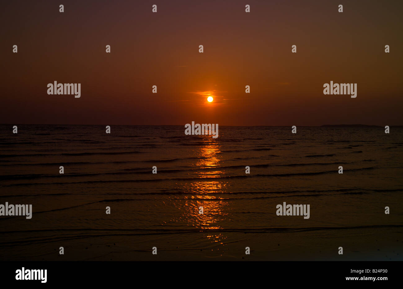 sun setting above the water with reflections in water Stock Photo - Alamy