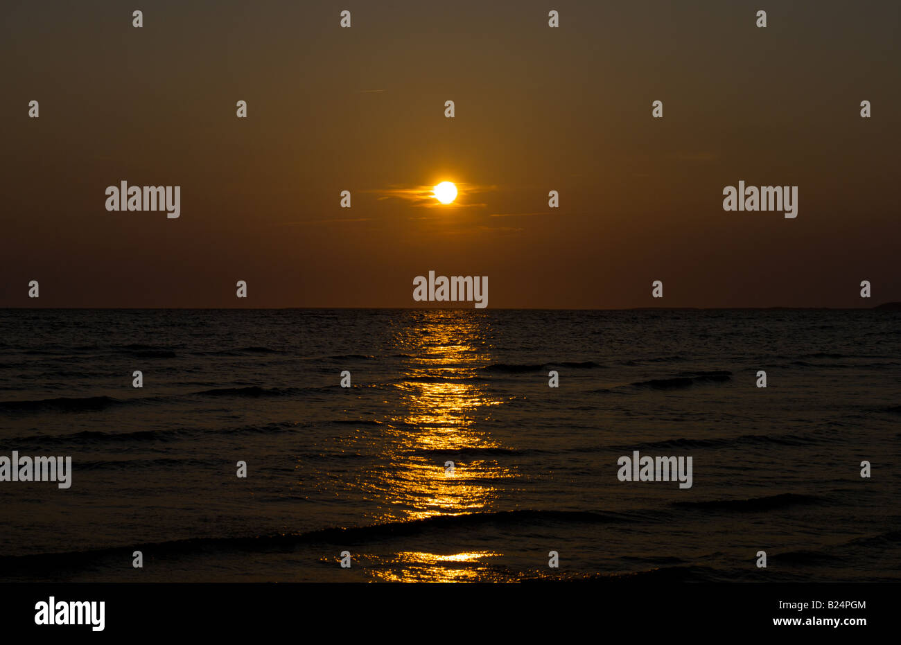 sun setting above the water with reflections in water Stock Photo - Alamy