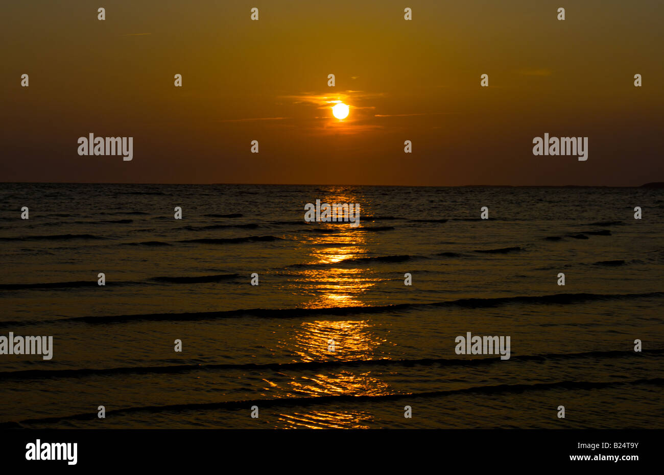 sun setting above the water with reflections in water Stock Photo - Alamy