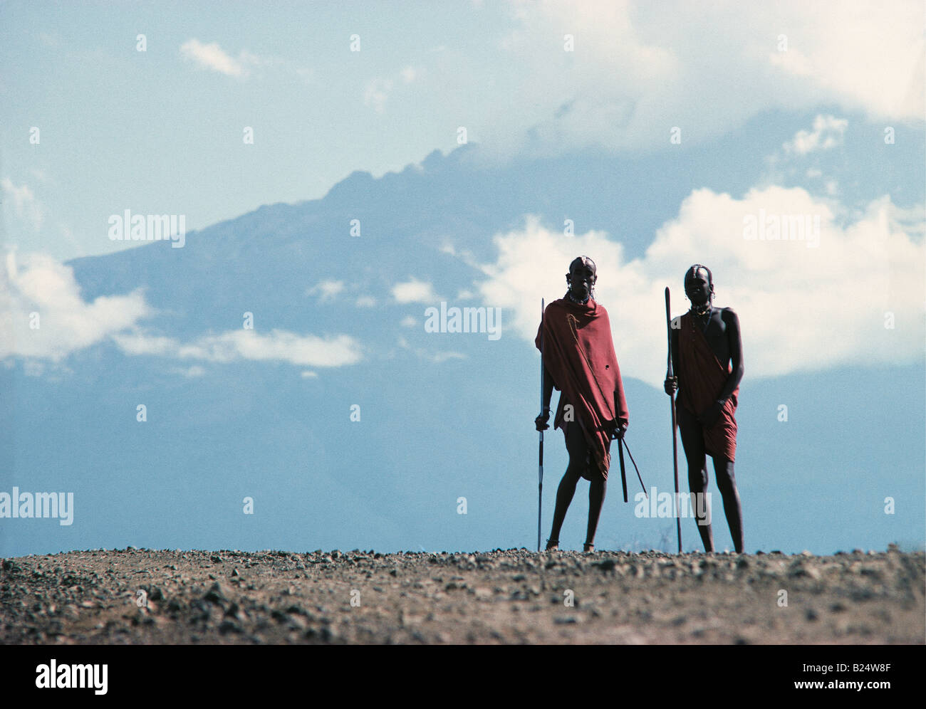 Two Maasai moran standing silhouetted with their spears and red cloaks ...