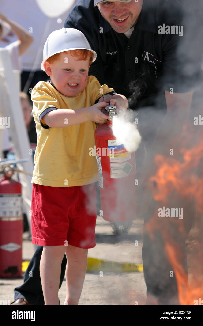 A young boy using a fire extinguisher on a fire under the direction of ...