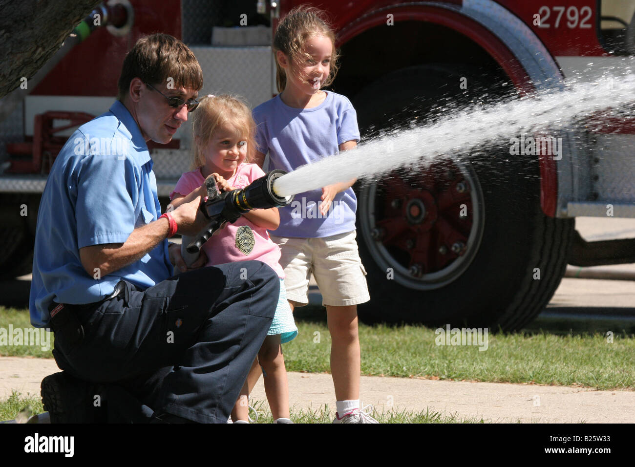 Two young girls using the fire hose under the direction of a ...