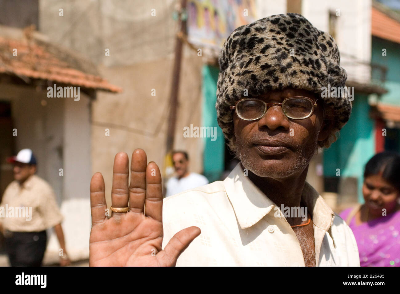 A bespectacled Indian man wearing a fur hat holds out his hand in ...