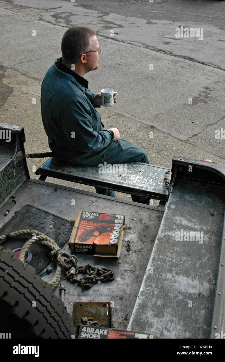 Car mechanic having a morning break on the loadbed of a 1950's Land ...