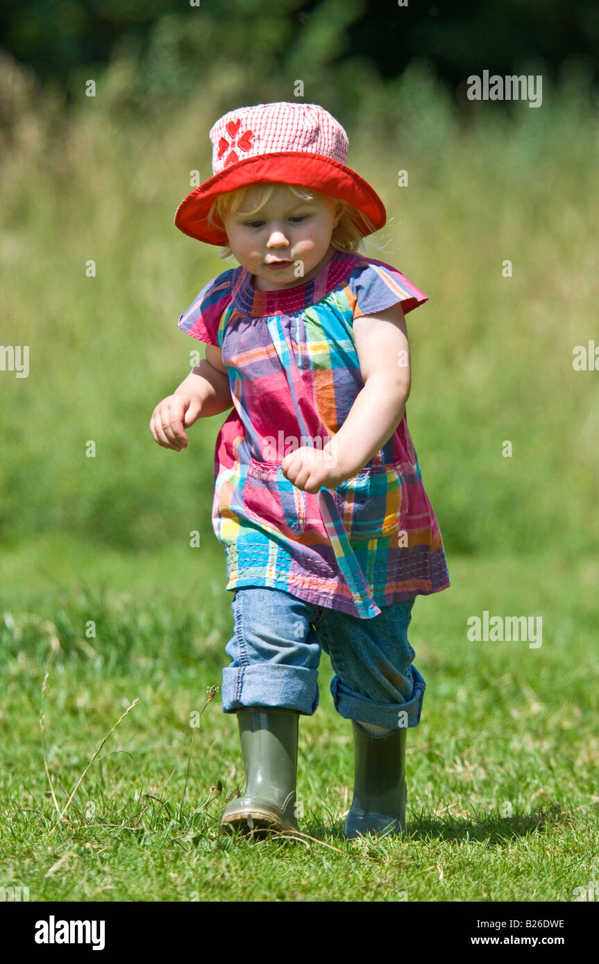 A cute young girl toddler running walking wearing wellies and a red sun ...