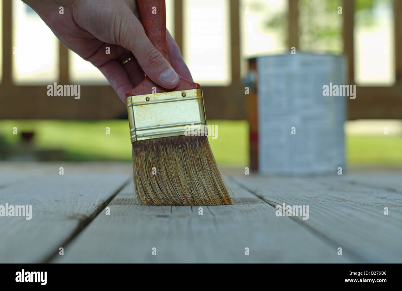 Man holding a brush while staining cedar deck floor can in background ...