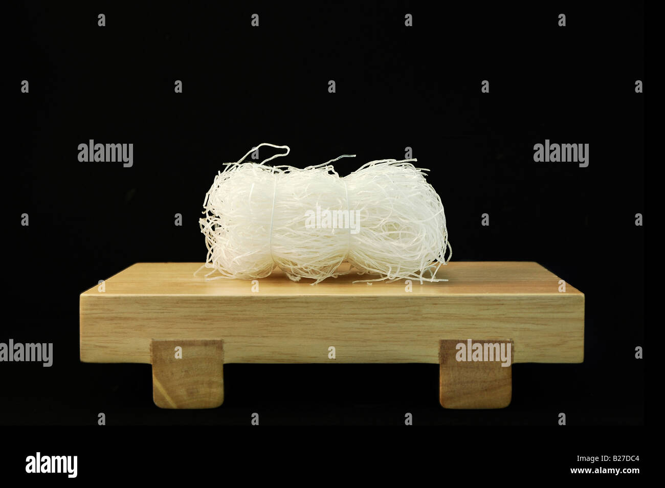Dried rice noodles on a wooden sushi block isolated on a black ...
