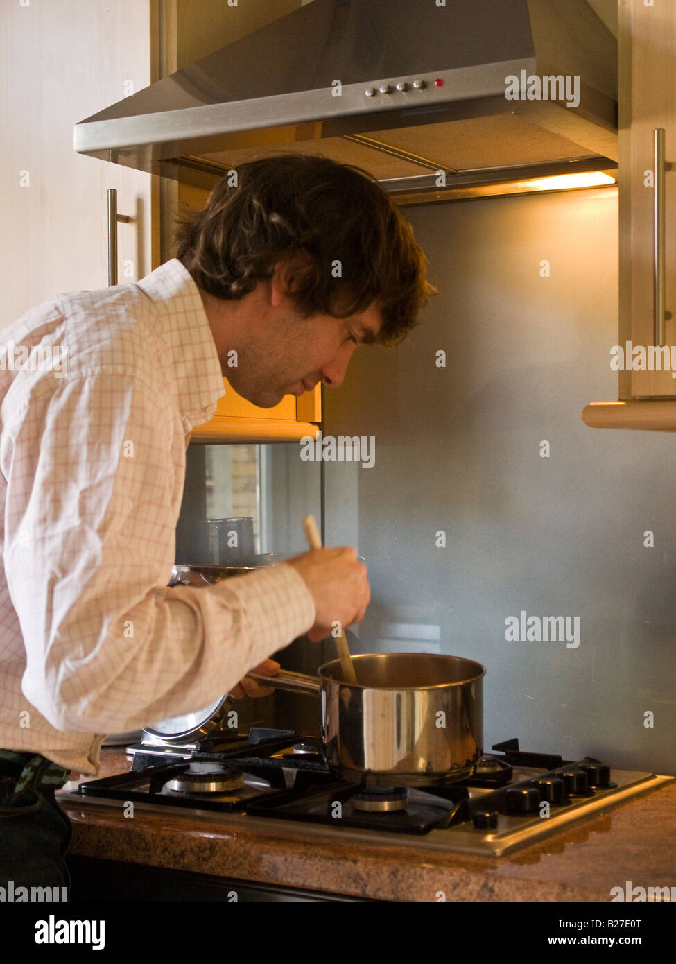 Thirtysomething white male cooking in a kitchen, stirring a pan with a ...