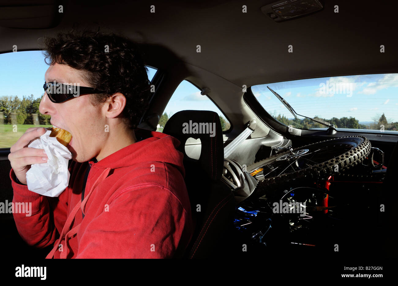 young man driving a car while eating Stock Photo - Alamy