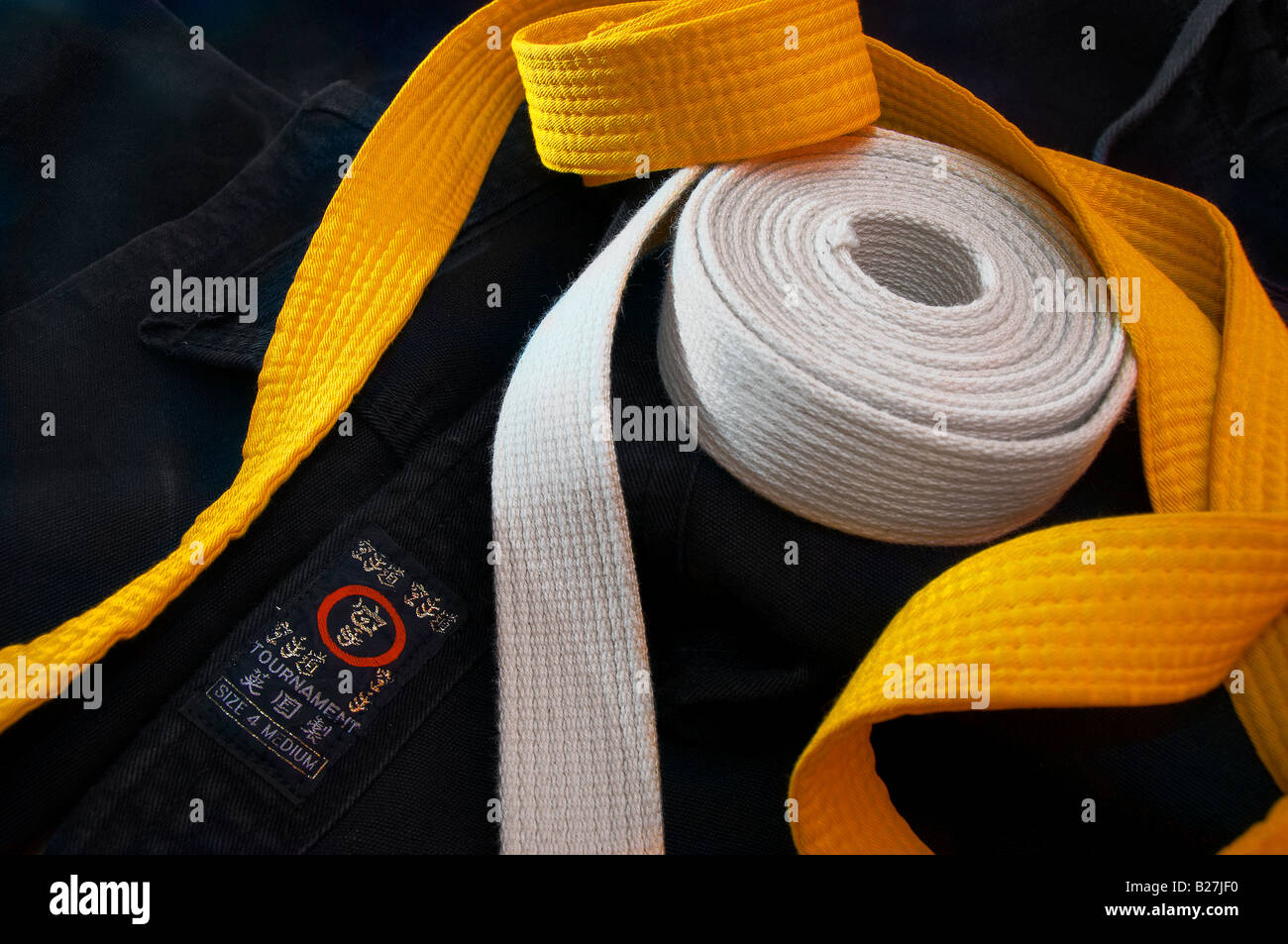 White and yellow karate belts coiled on a folded black gi Stock Photo ...