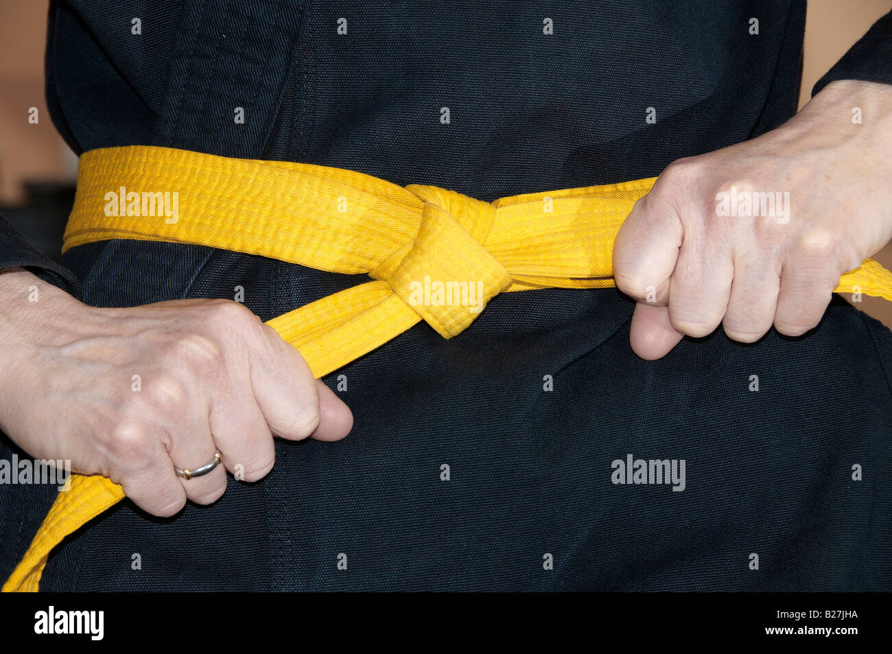 Girl in karate gi tightening yellow belt Stock Photo - Alamy
