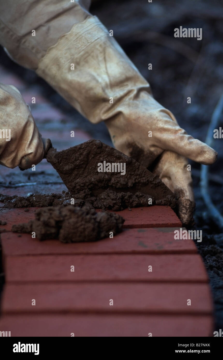 The gloved hands of a Mason using a trowel to place mortar between red ...