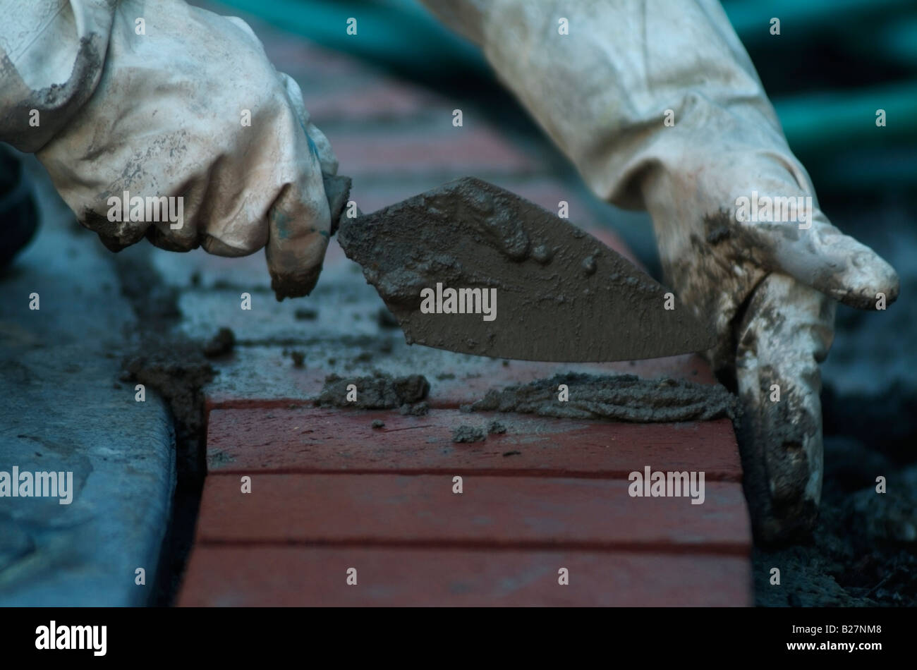 The gloved hands of a Mason using a trowel to place mortar between clay ...