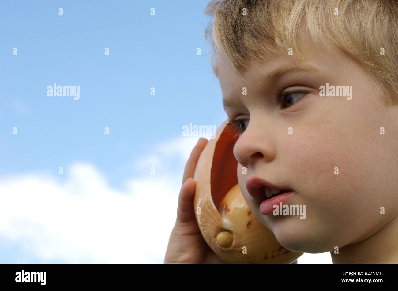 Boy holding a Seashell to his ear Stock Photo - Alamy