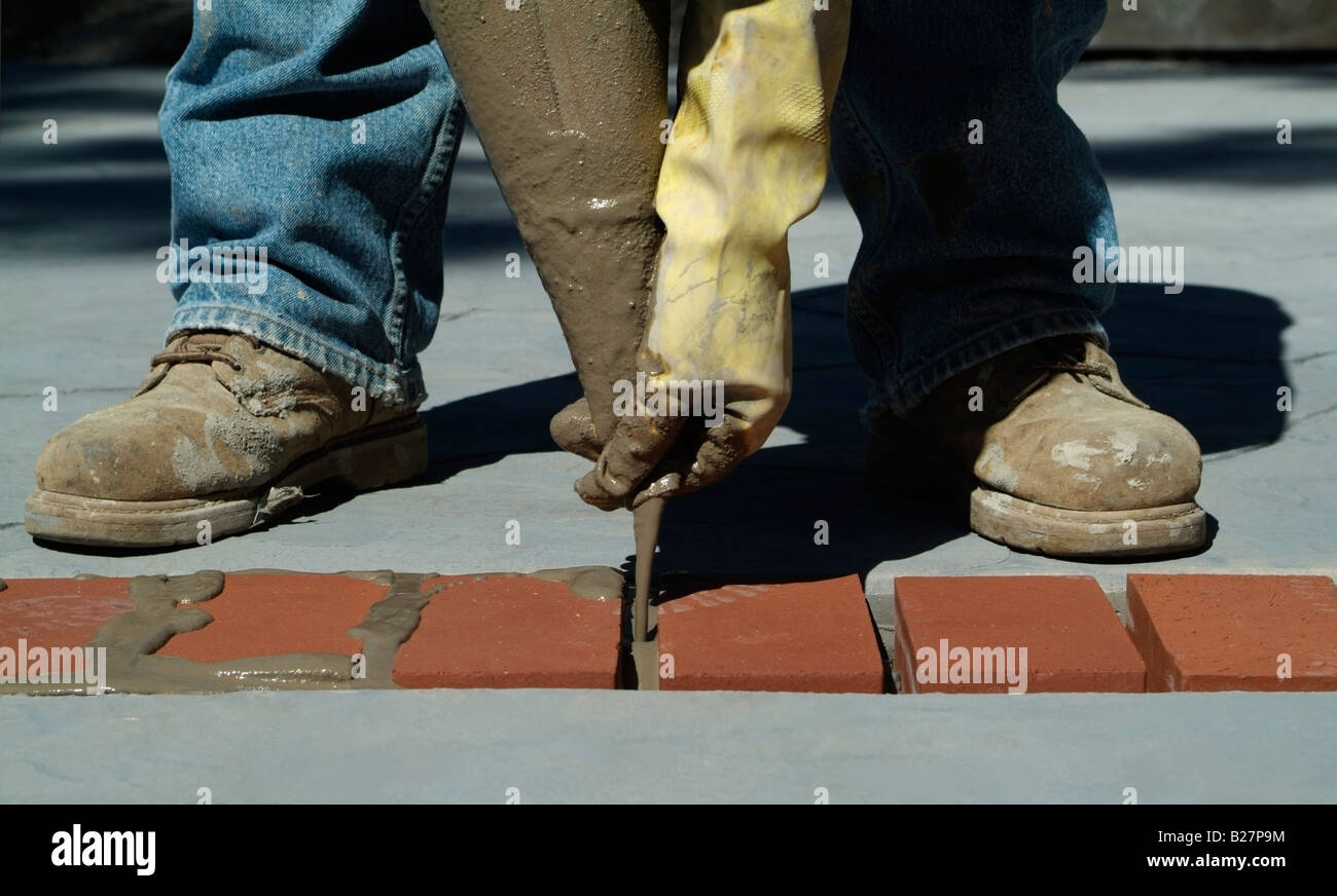 Mason using a large sieve to place wet mortar between red clay bricks ...