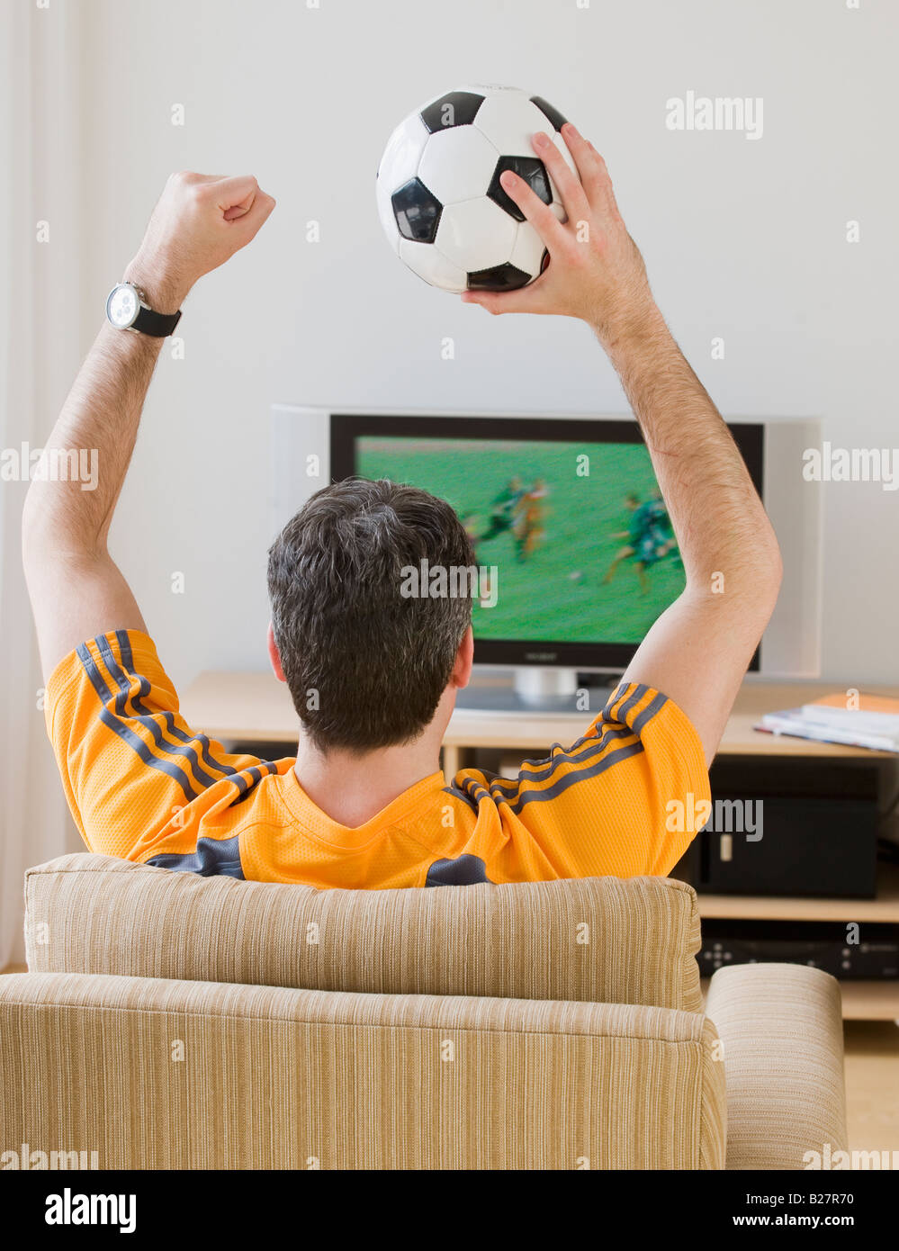 Man with soccer ball cheering at television Stock Photo - Alamy
