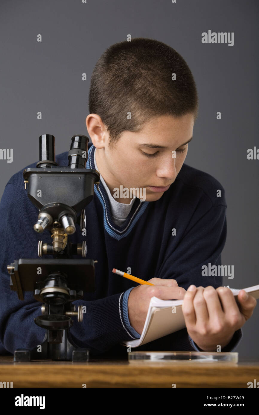 Boy writing in notebook next to microscope Stock Photo - Alamy