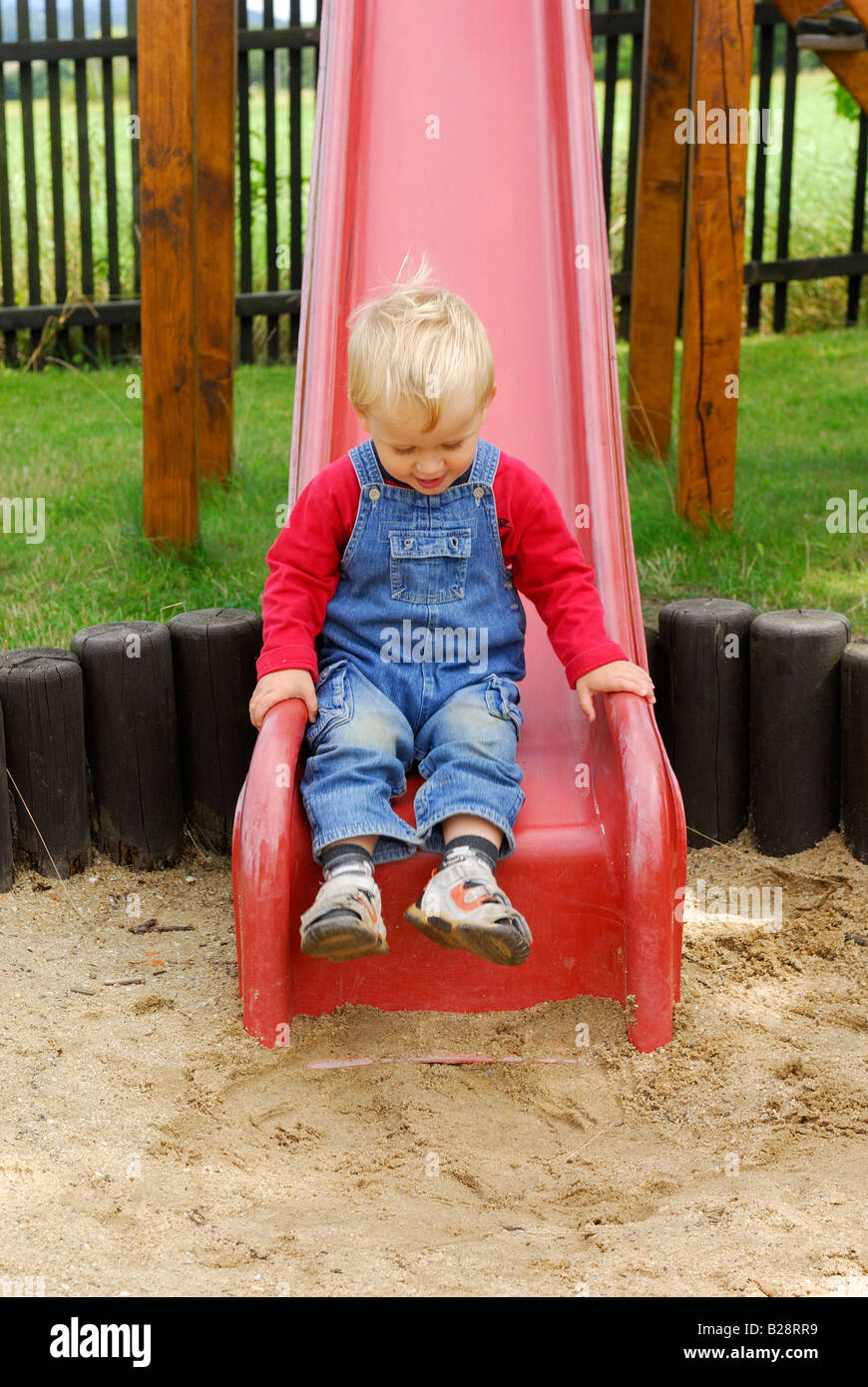 Baby blonde boy sliding down the slide on the playground Stock Photo ...