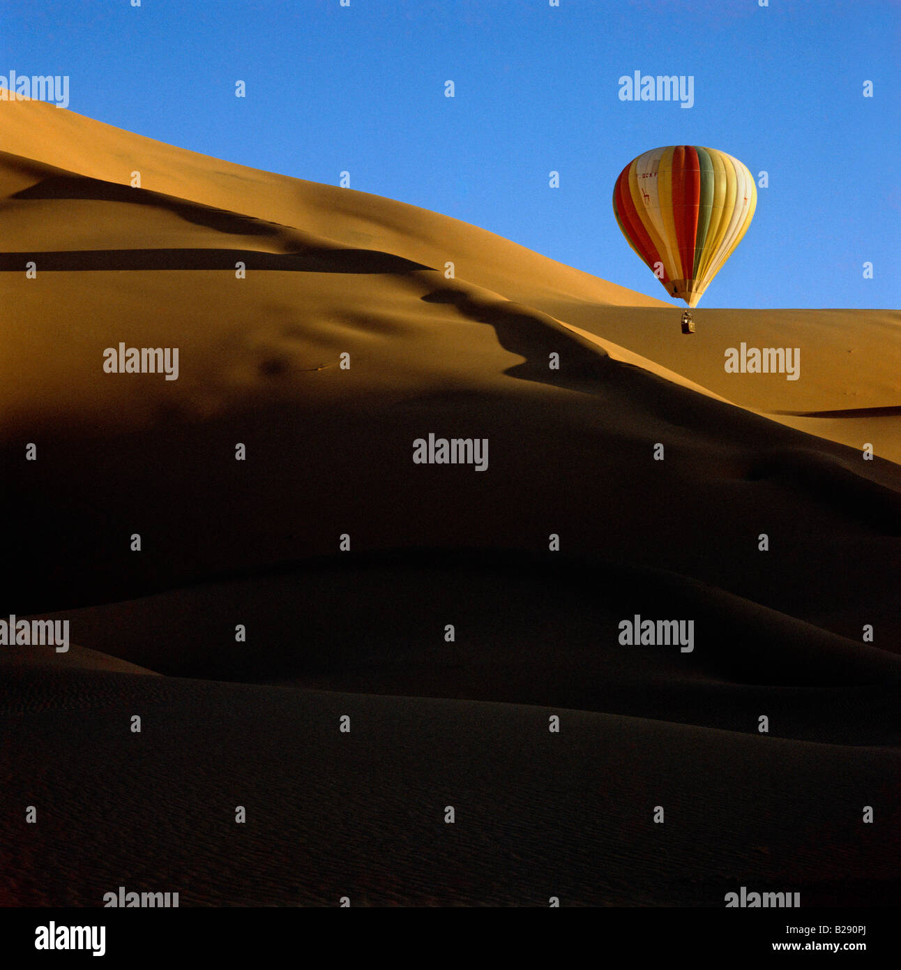 Balloon flying over desert in front of very high sand dune at sunset ...