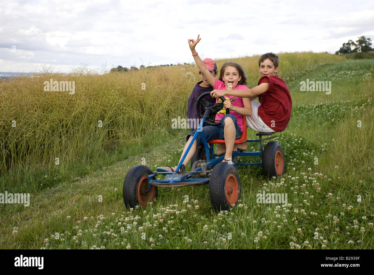 Boy and girl having fun on pedal go cart in farm field Cotswolds UK ...