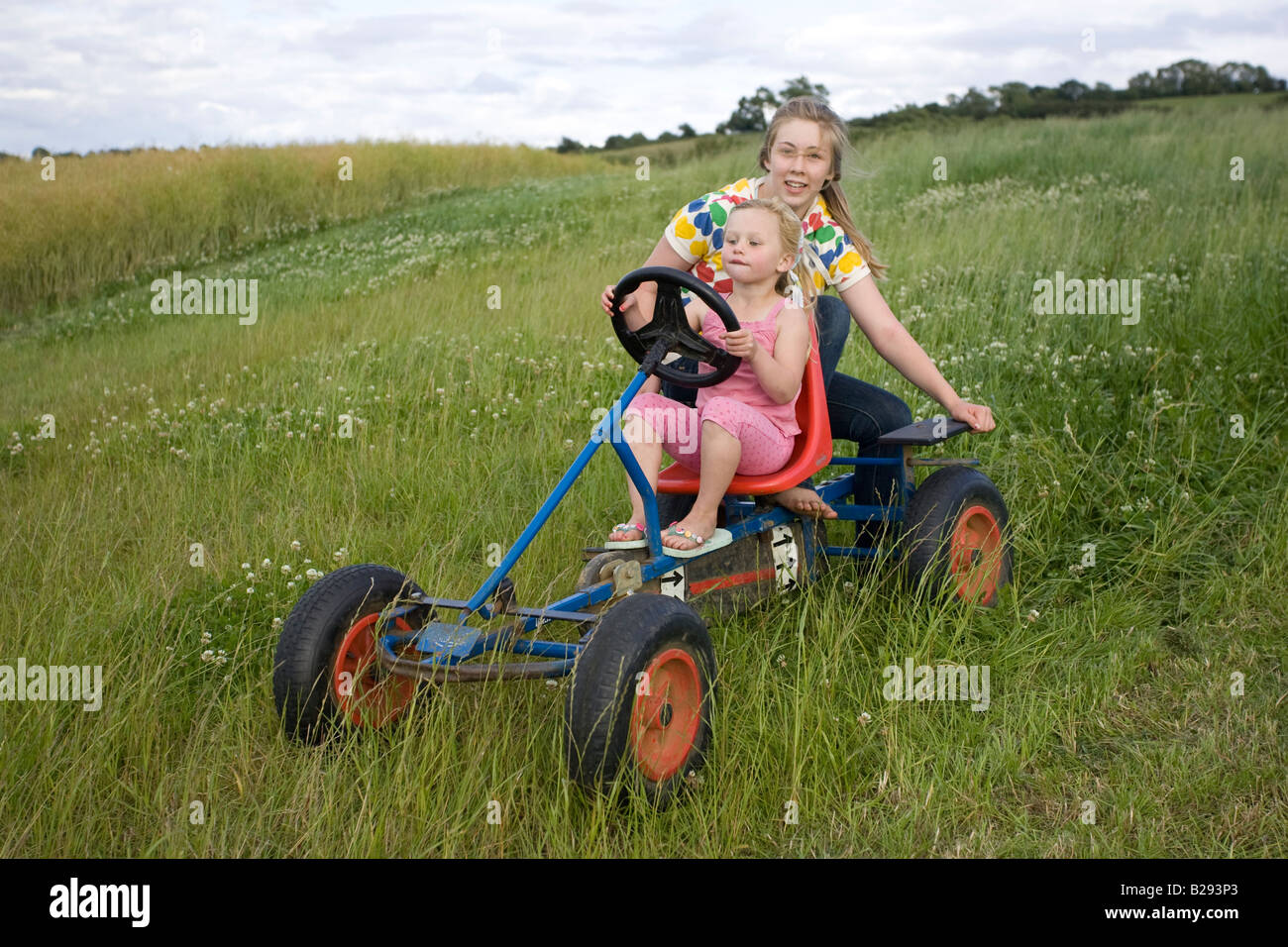 Two girls having fun on pedal go cart in farm field Cotswolds UK Stock ...
