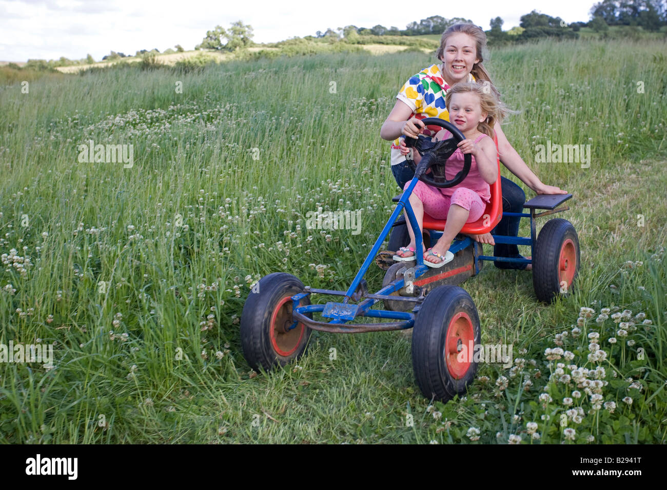 Two girls having fun on pedal go cart in farm field Cotswolds UK Stock ...