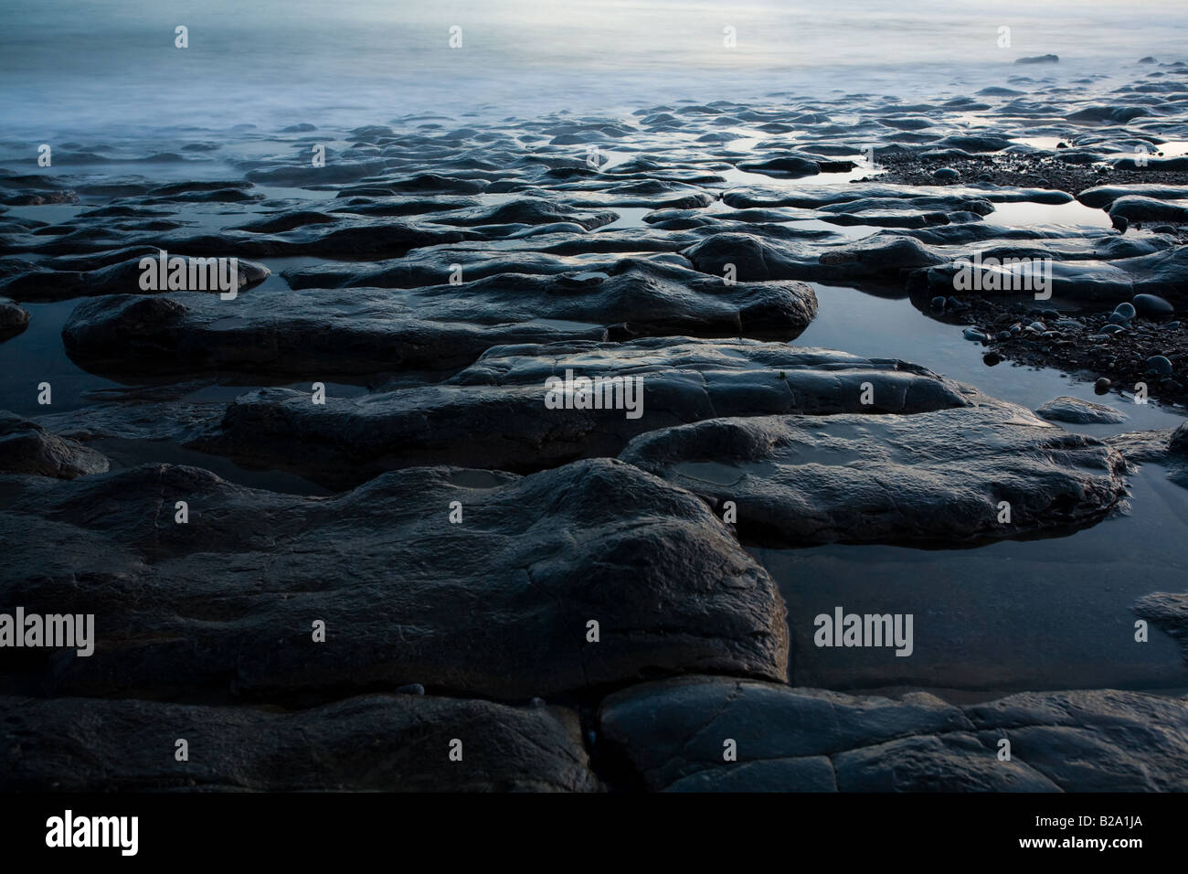 Evening reflections on the rocks on a beach Stock Photo - Alamy