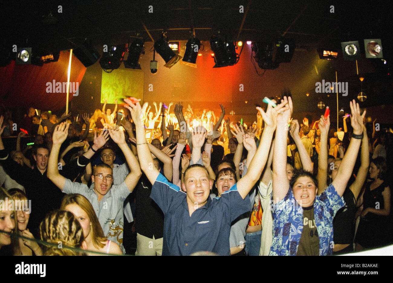 Caucasian teenagers in a packed nightclub dancing with their arms in ...