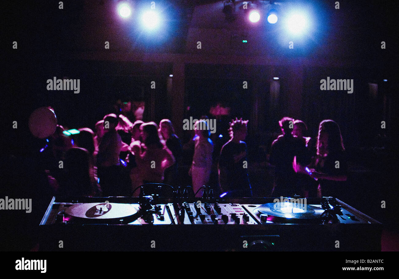 Crowded dance floor in a nightclub, seen from behind a DJ mixer and ...