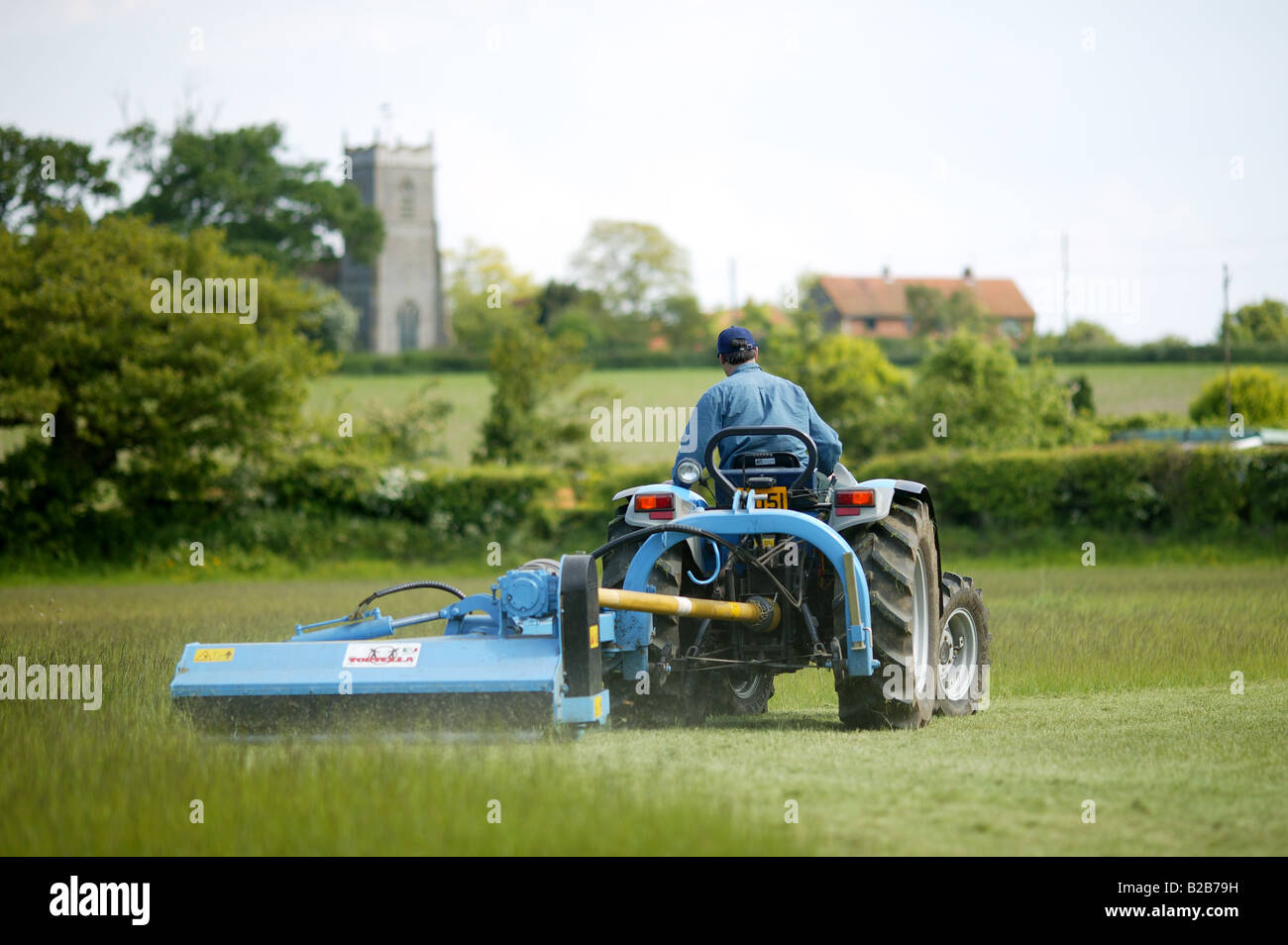 Farmer mowing a pasture with the village church in the distance "North ...