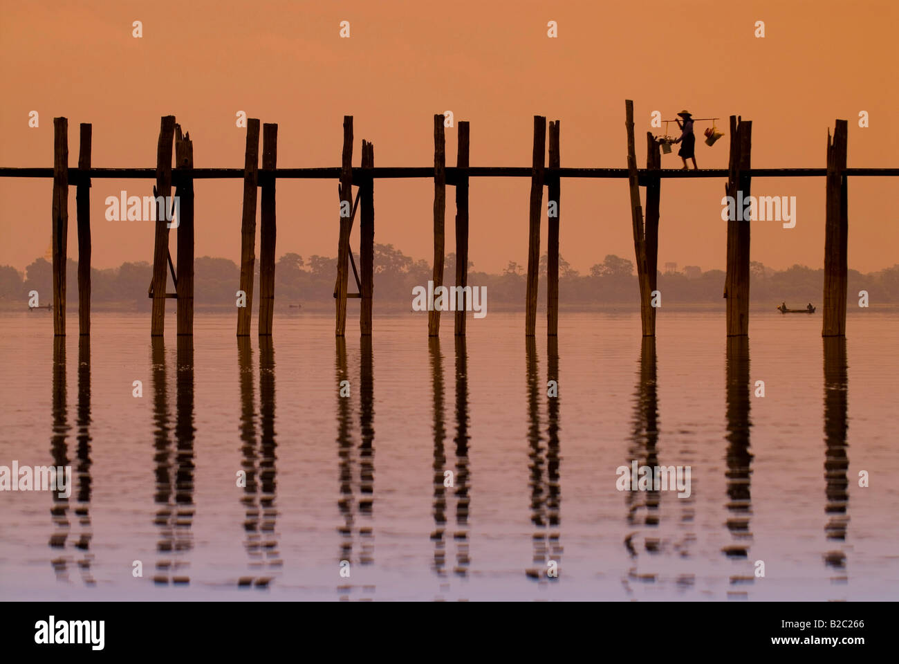 Man carrying a load crossing the U Bein Bridge at sunset, old wooden ...