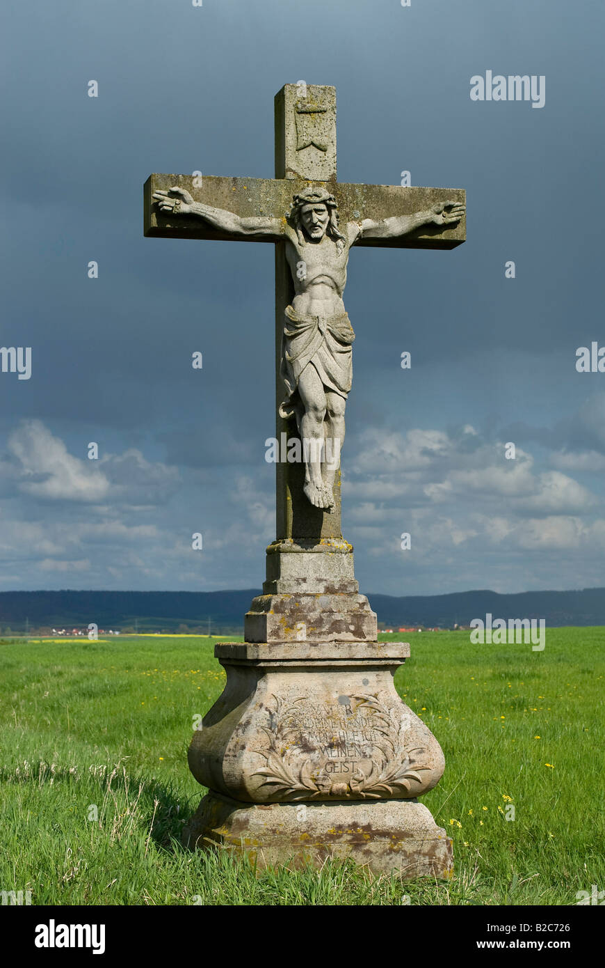 Jesus on the cross, stone statue in a field beneath storm clouds ...