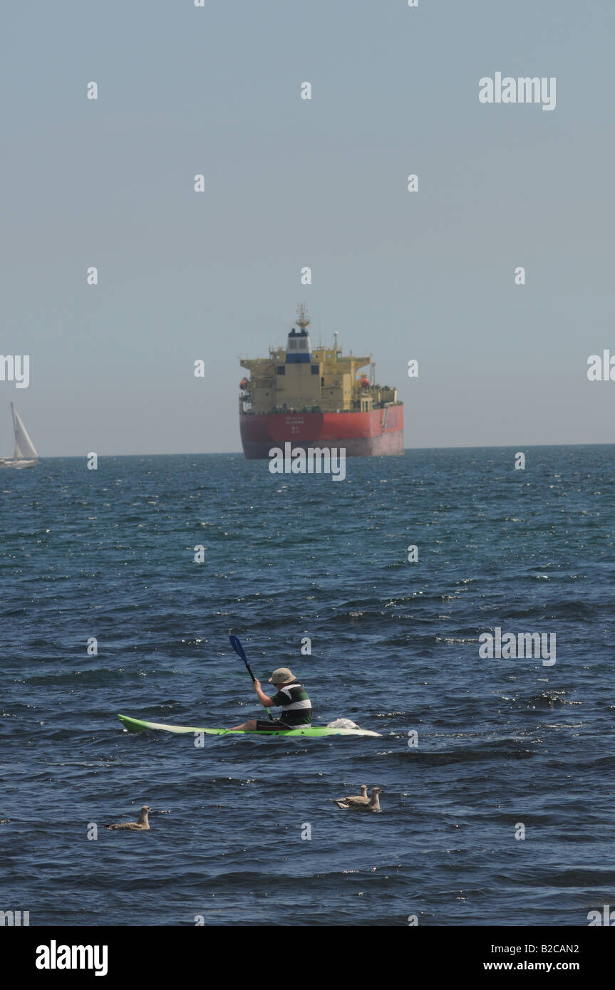 A kayak is paddled off a beach in Cornwall with an oil tanker in the ...