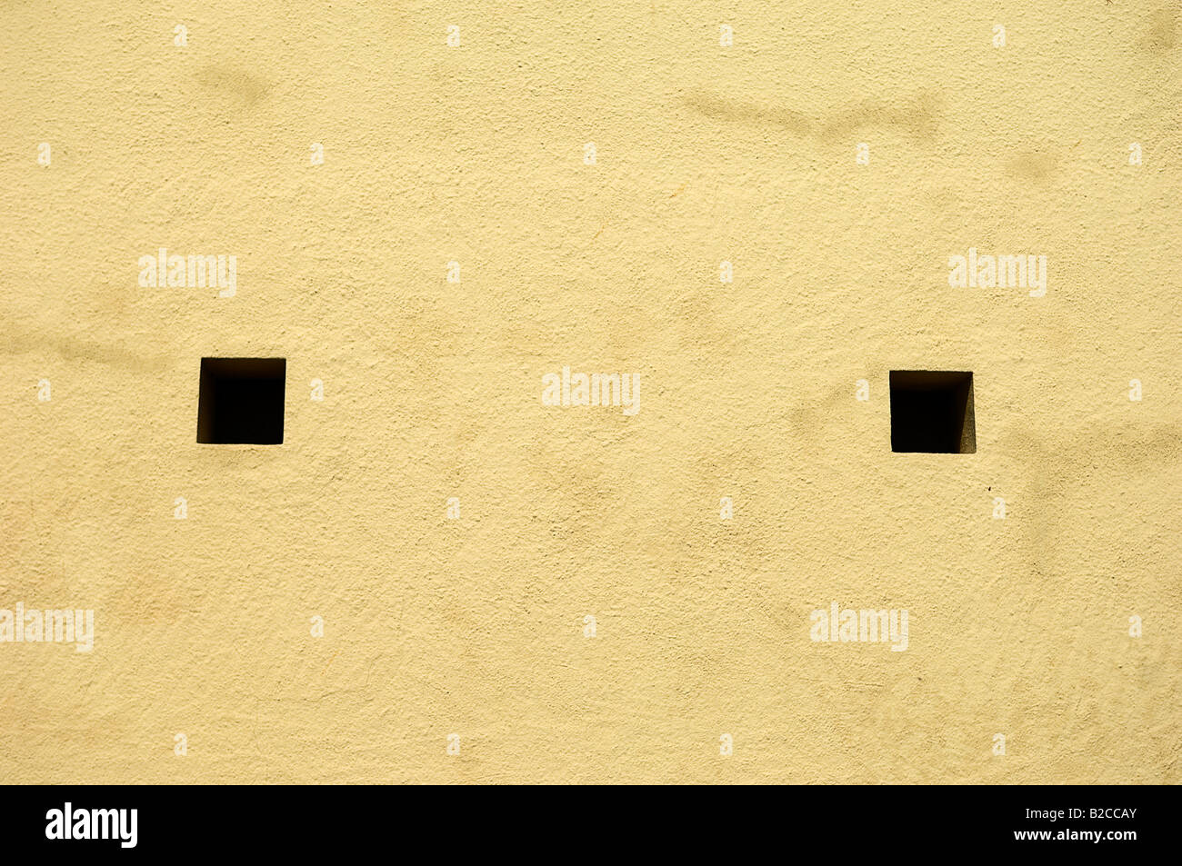 Detail of a rugged yellow wall with two square loopholes Stock Photo ...