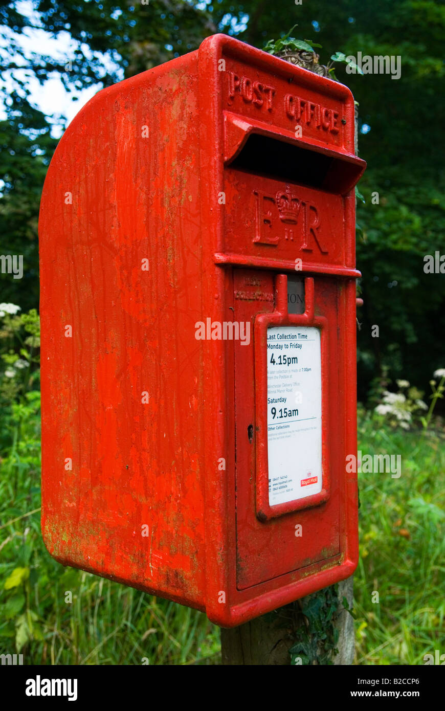 Royal Mail red roadside mailbox fixed to a wooden post in neglected ...