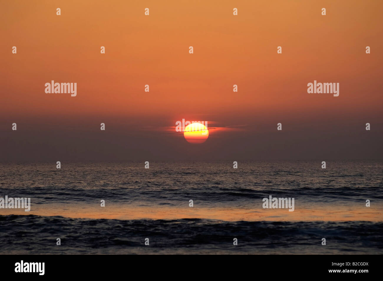 Red sun as it sets over the calm ocean waters Stock Photo - Alamy
