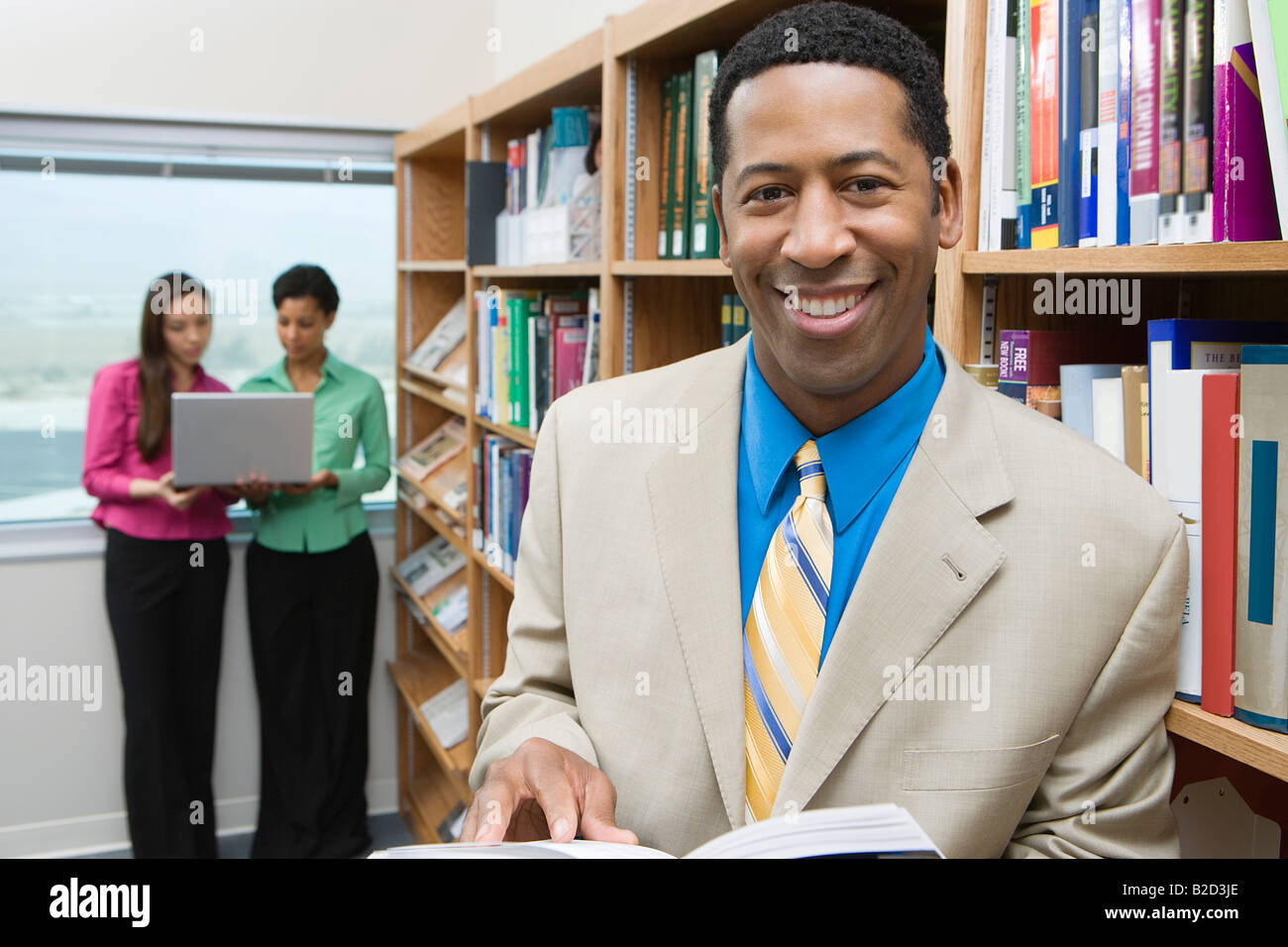 Portrait of man with book in library, two women in background Stock ...