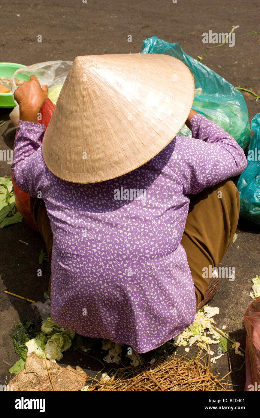 A woman in a conical straw hat squats a street in Cholon, Vietnam Stock ...
