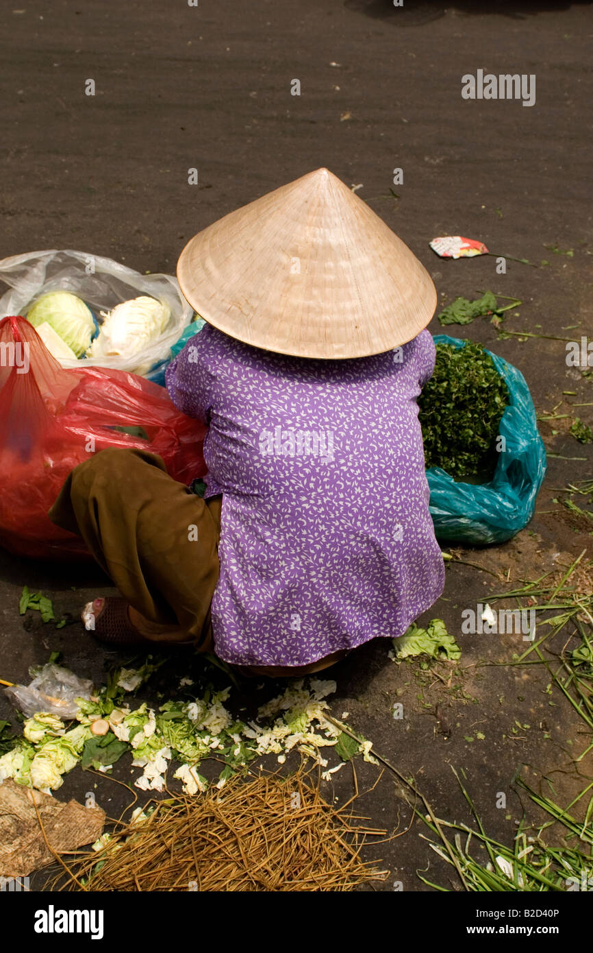 A woman in a conical straw hat squats a street in Cholon, Vietnam Stock ...