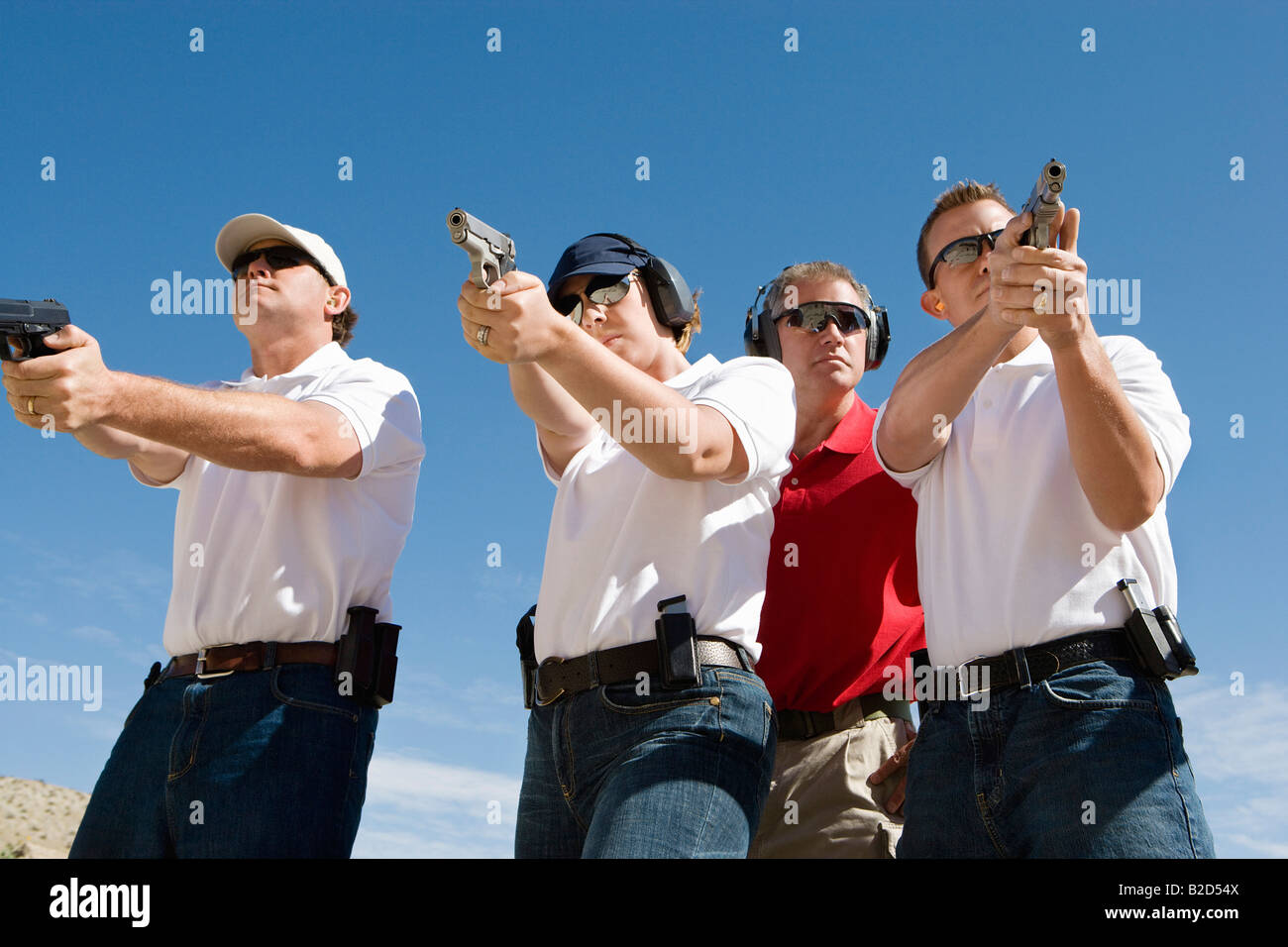 Instructor assisting people aiming guns at firing range Stock Photo - Alamy